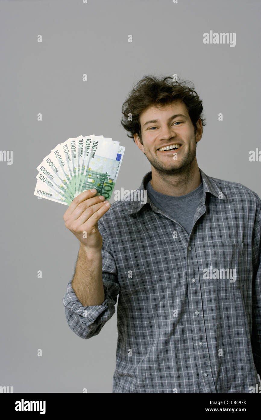 Young man holding 100 Euro bills against grey background Stock Photo ...