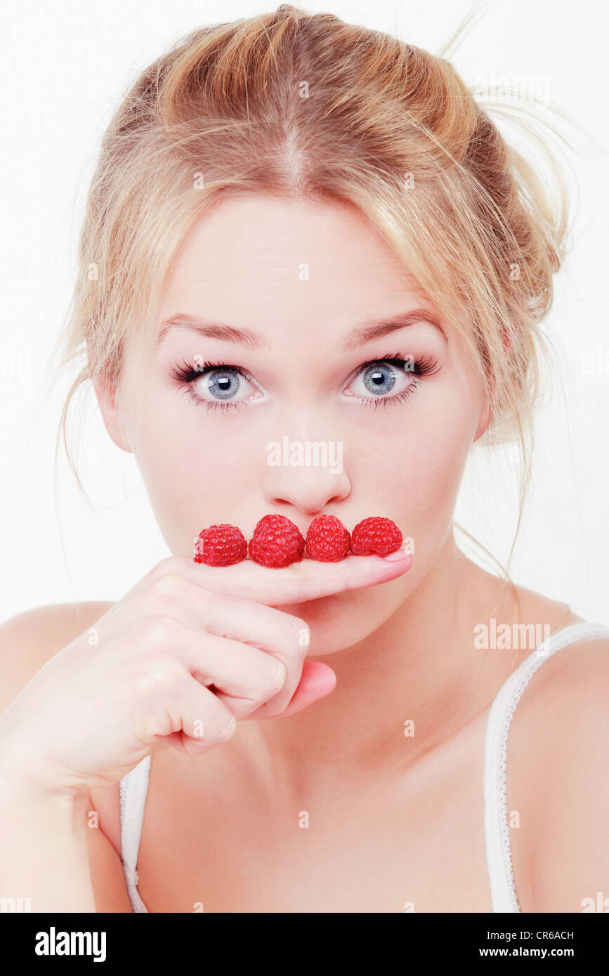 Young woman making moustache with raspberries on her finger, portrait ...