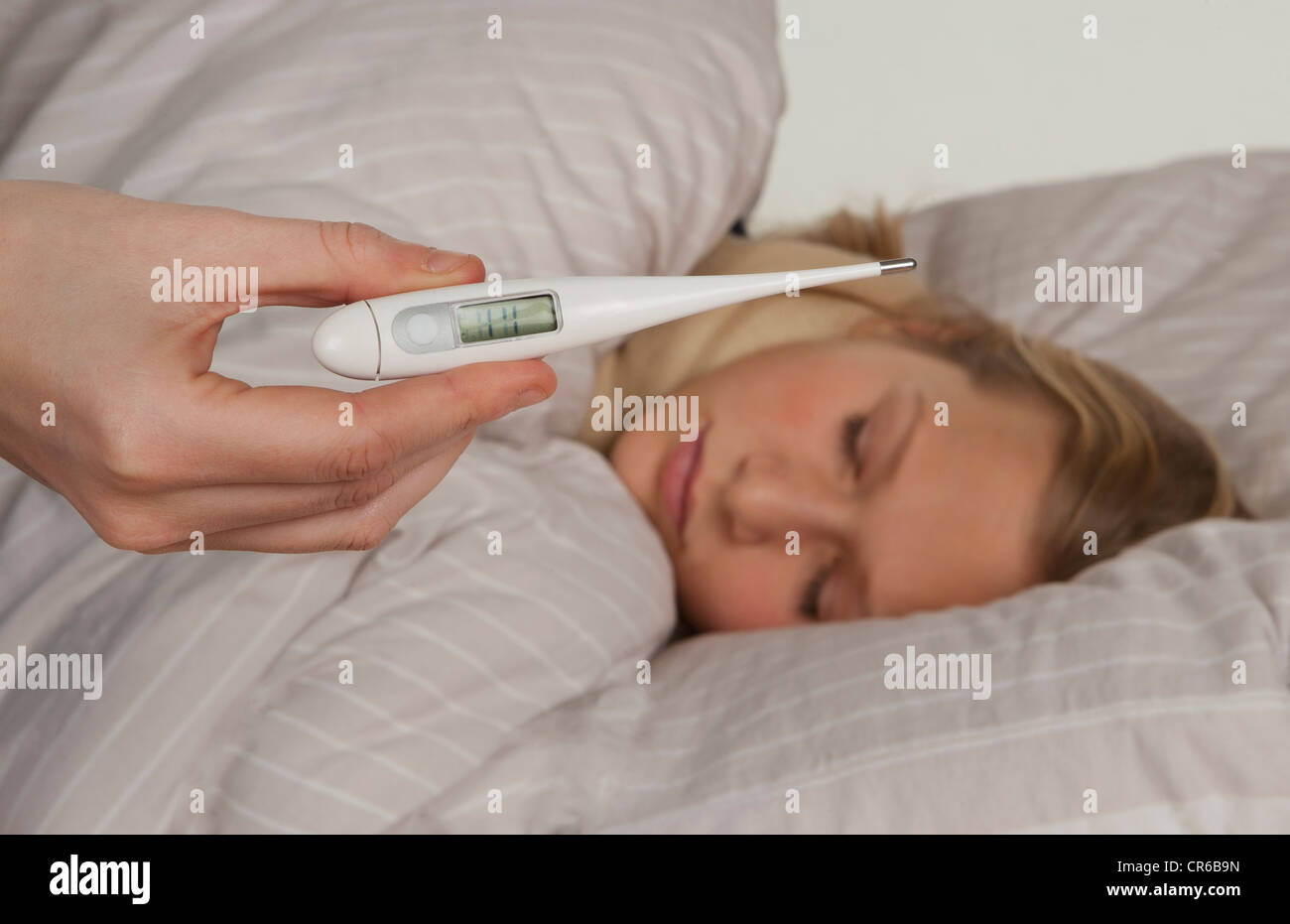 Female doctor showing digital thermometer, teenage girl in background ...