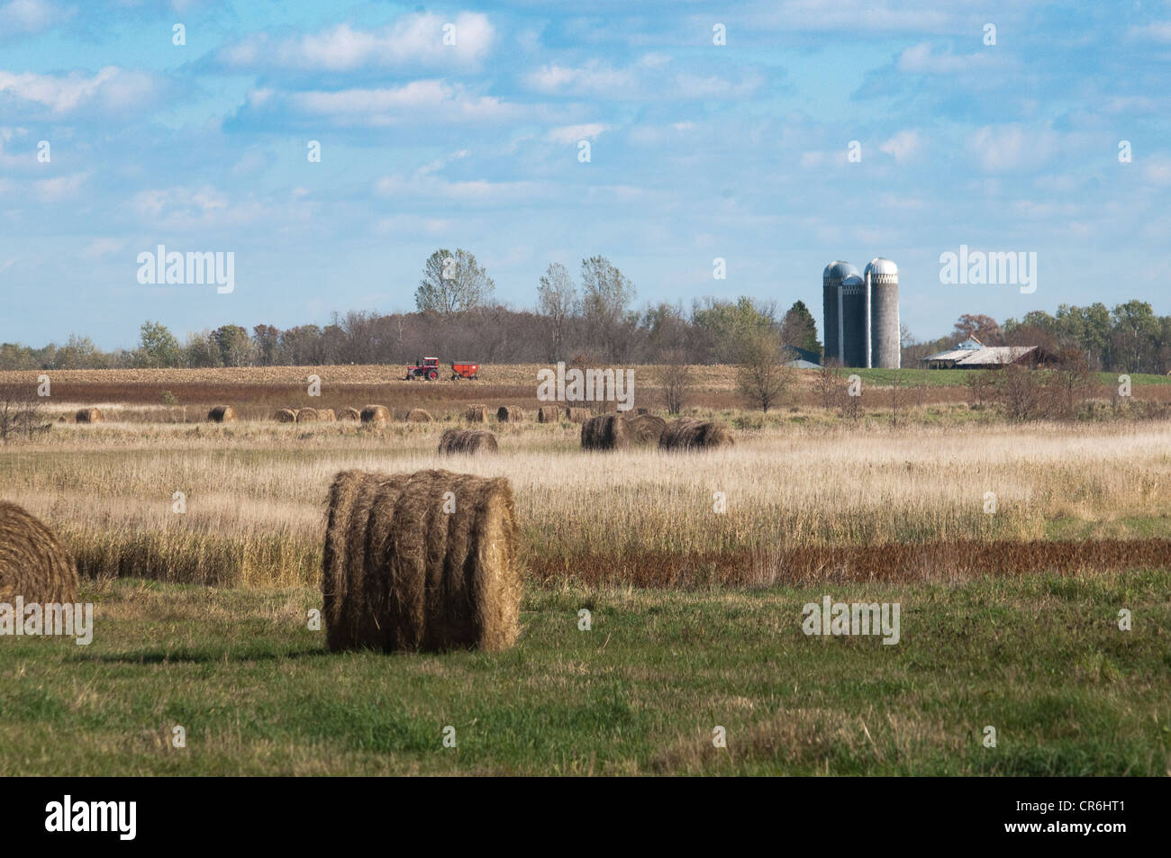 bales of hay in foreground with red tractor and silos in background ...