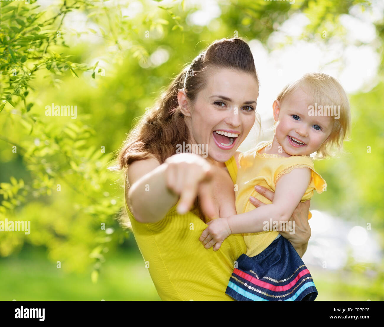 Portrait of baby girl and smiling mother pointing in camera Stock Photo ...