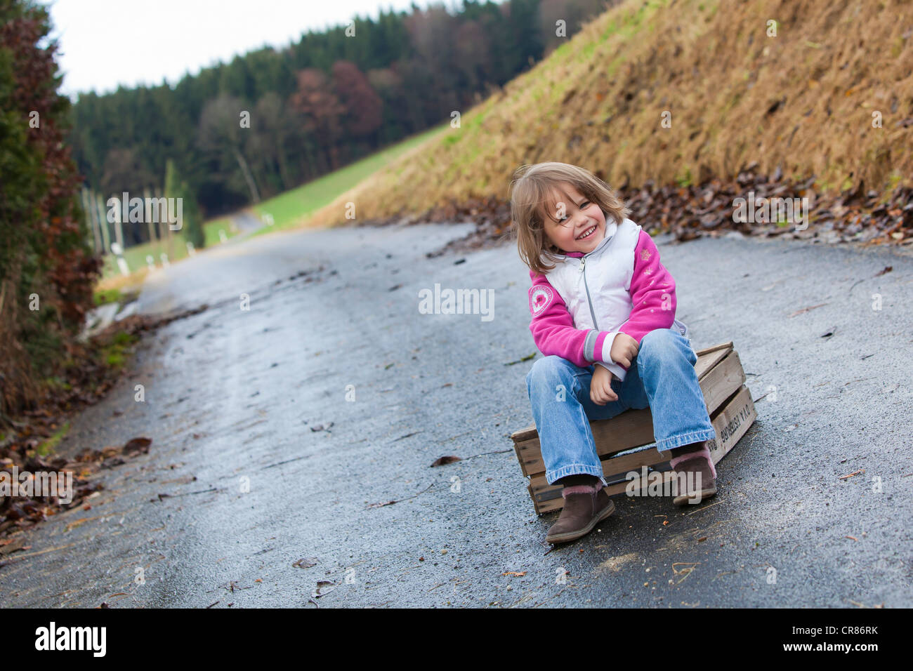 Girl, 4, sitting on a wooden crate on a path Stock Photo - Alamy