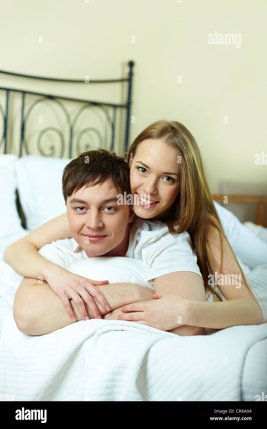 Happy girl embracing her boyfriend in bed and both looking at camera ...