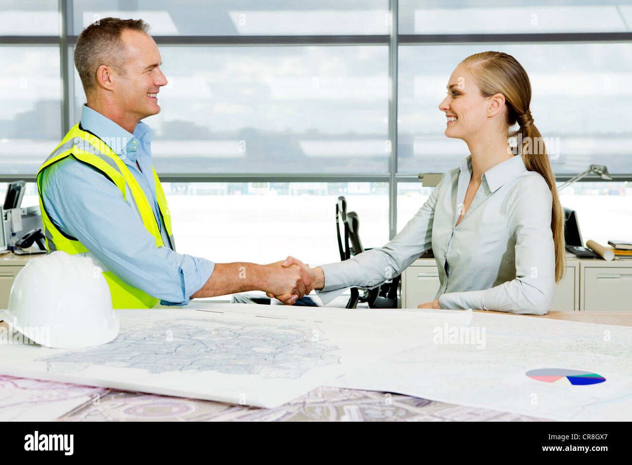 Engineer shaking hands with architect at desk of blueprints in office ...