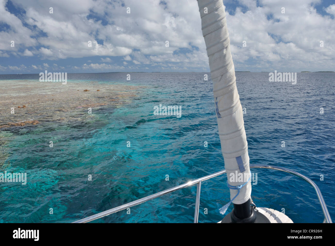 A yacht motors past coral heads, with the sun overhead, in Makemo atoll ...
