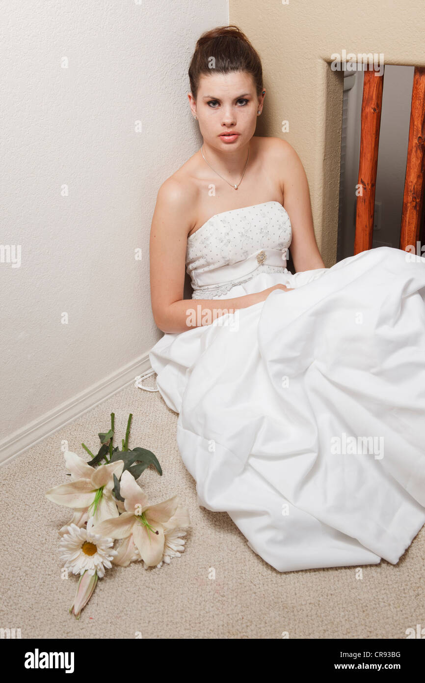 Nervous young bride wearing a wedding gown, sitting on an interior ...