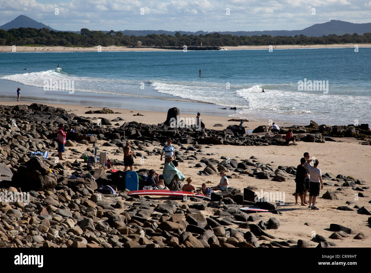 Tourists relaxing on rocks at beach, mountain in distant, Sunshine ...