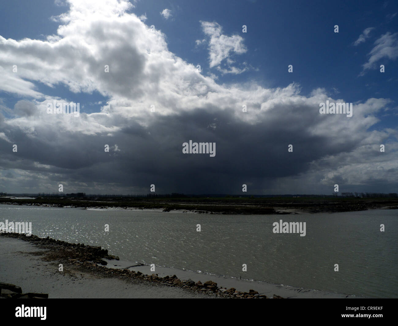Black storm cloud with silvery lining, sun and blue sky, shoreline ...