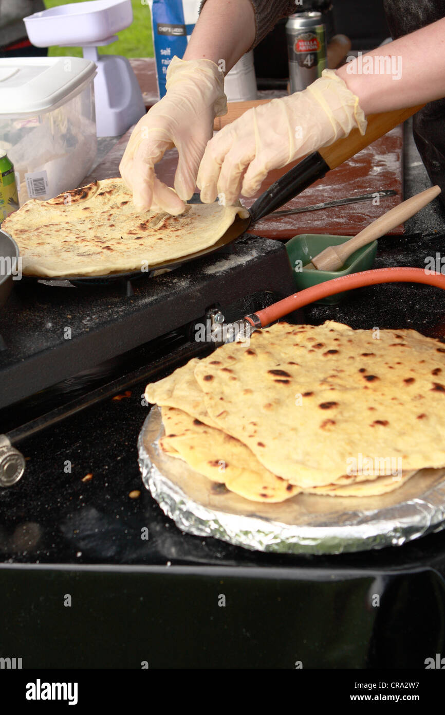 A small pile of rotis next to a roti being cooked on a portable gas ...