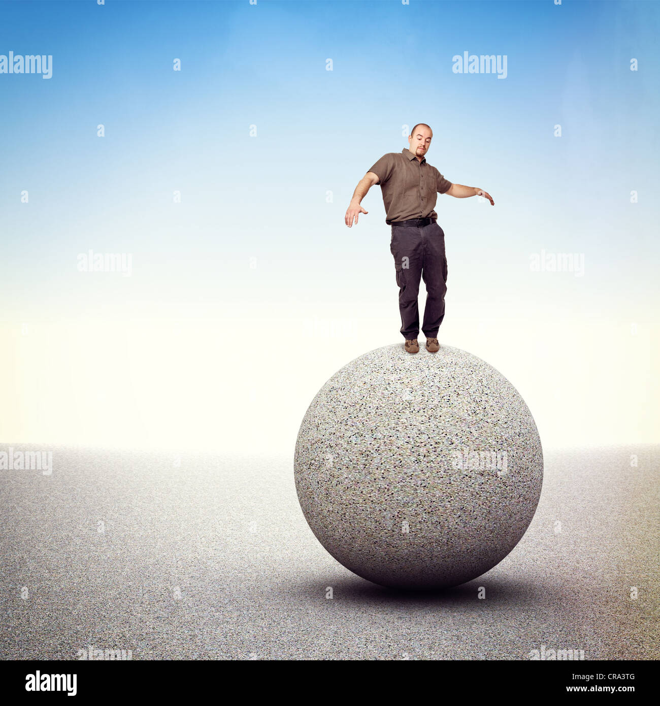 man try to balance himself isolated on big rock sphere Stock Photo - Alamy