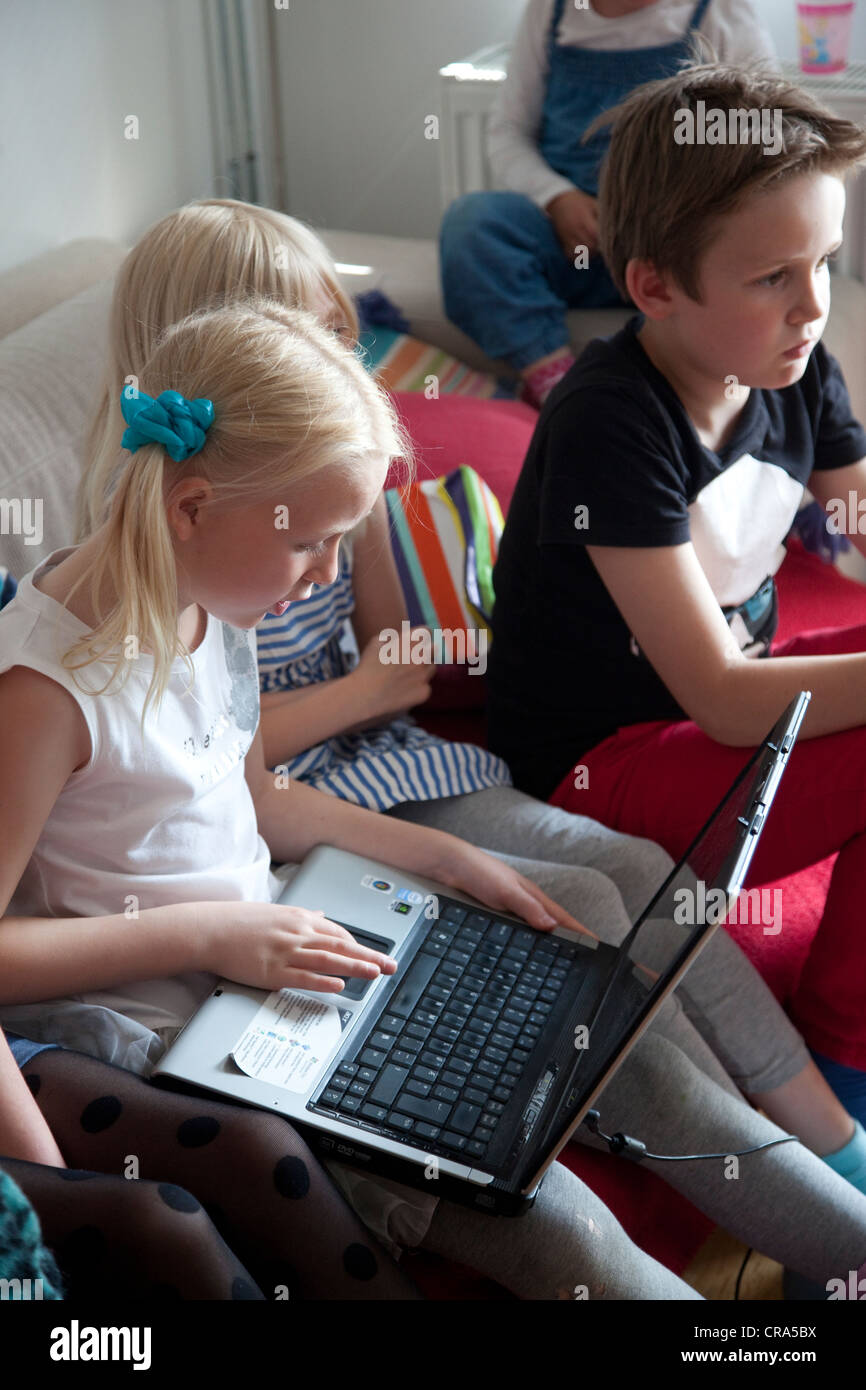 Children using a computer laptop whilst sitting together on sofa Stock ...