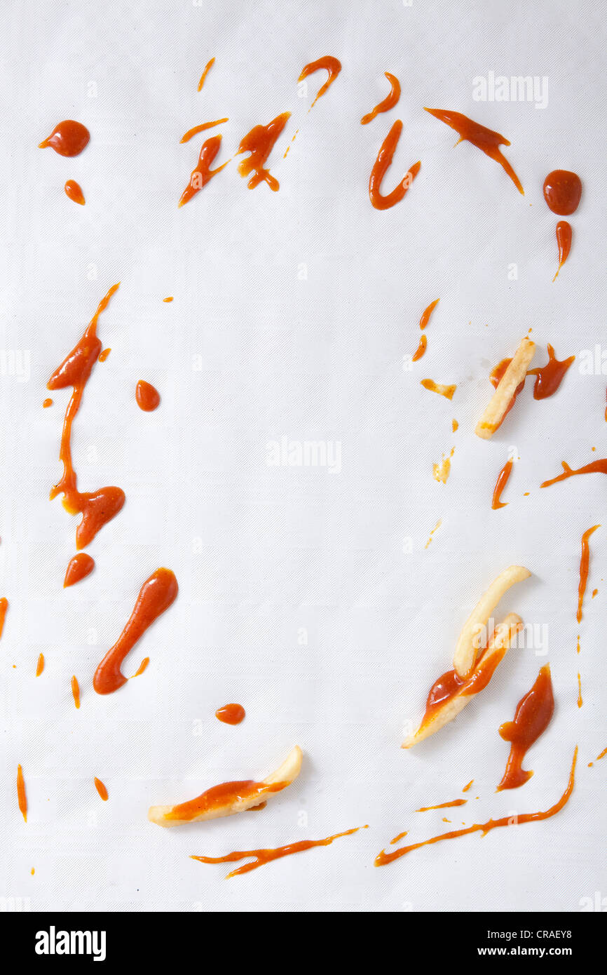 French fries and spilled ketchup on a paper table cloth, food scraps ...