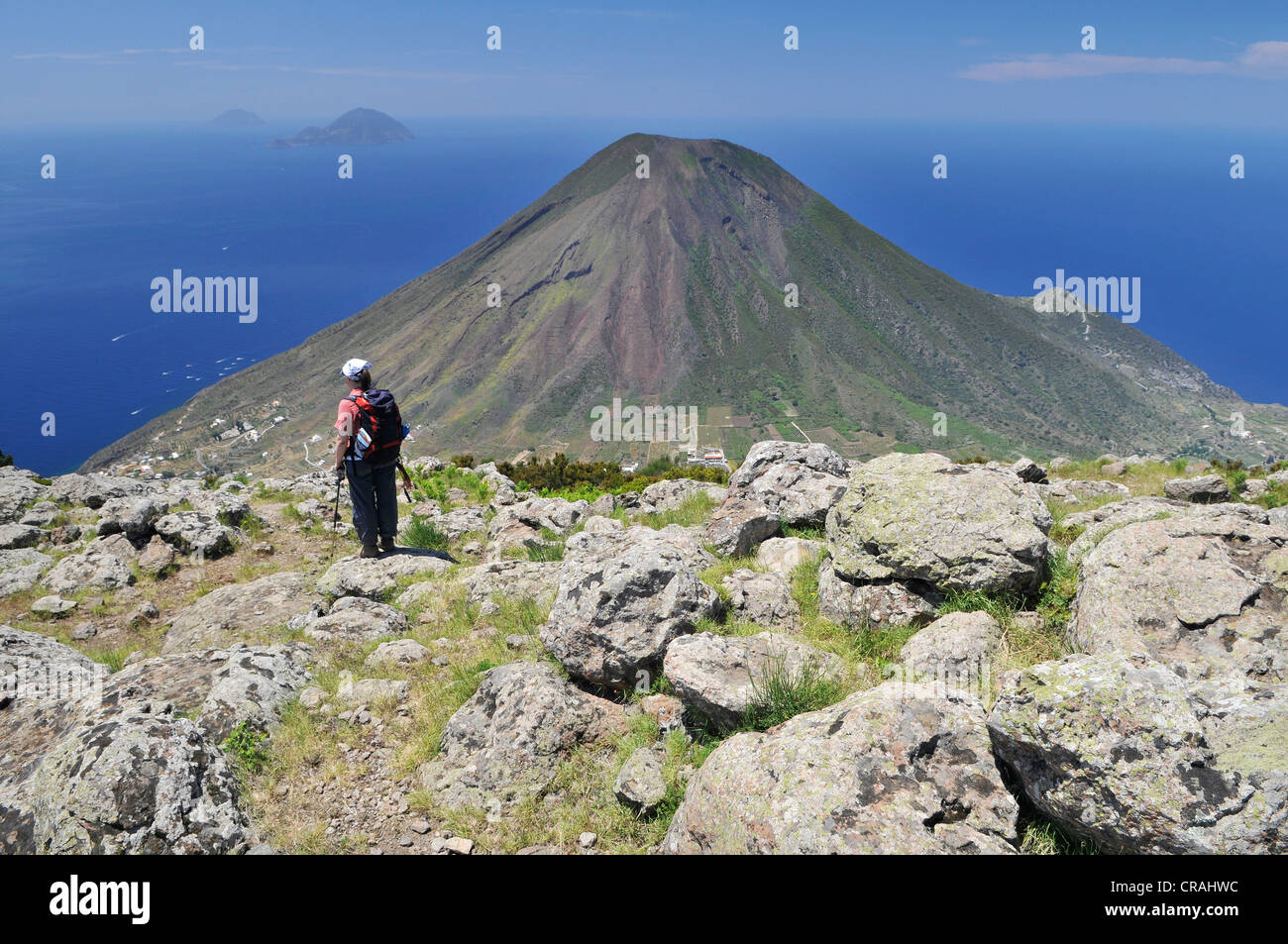 Hiker in front of a volcano on Salina, with the islands of Filicudi and ...