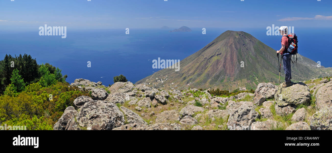 Hiker in front of a volcano on Salina, with the islands of Filicudi and ...