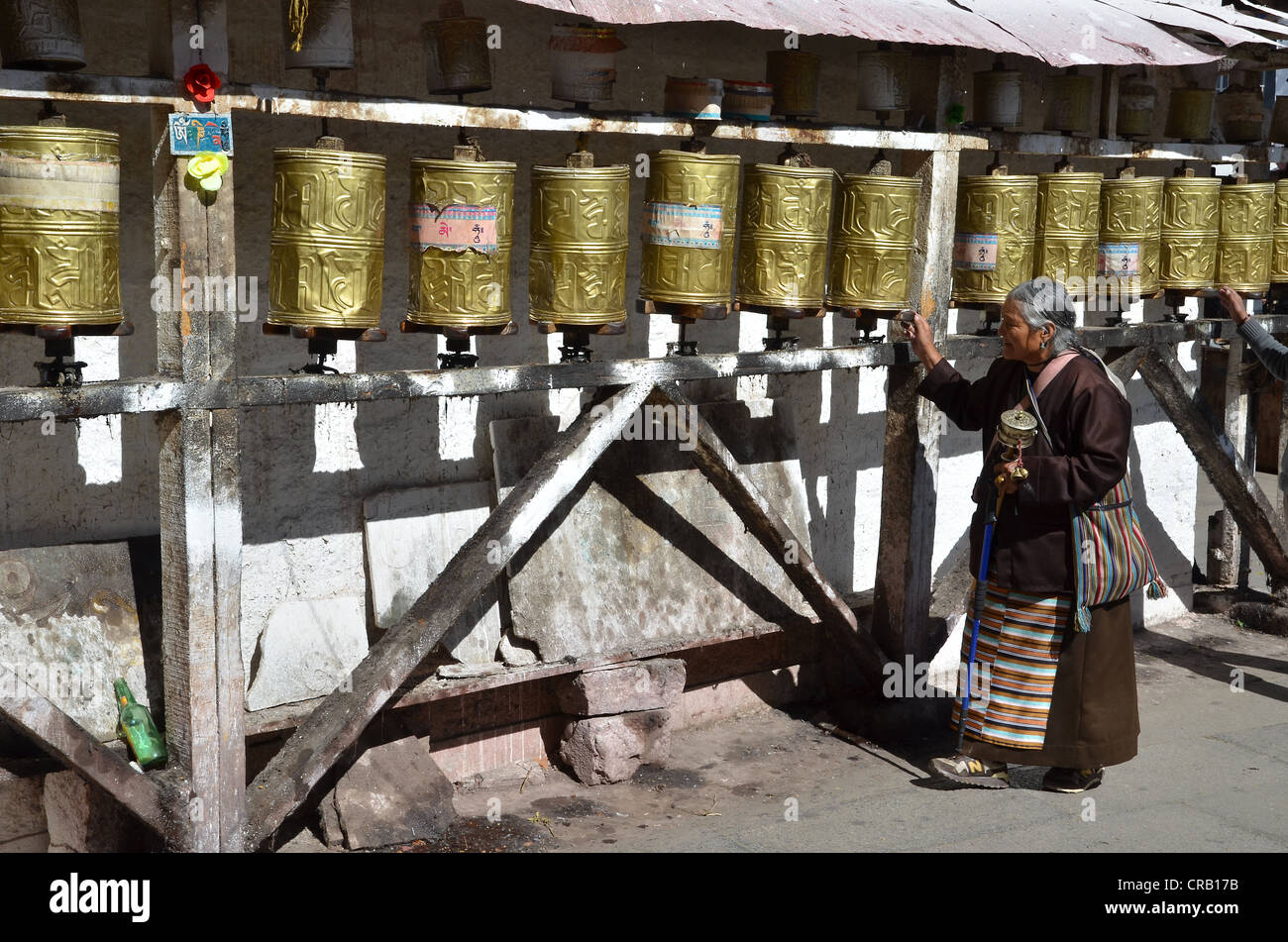 Elderly Tibetan woman in traditional costume surrounding a small temple ...