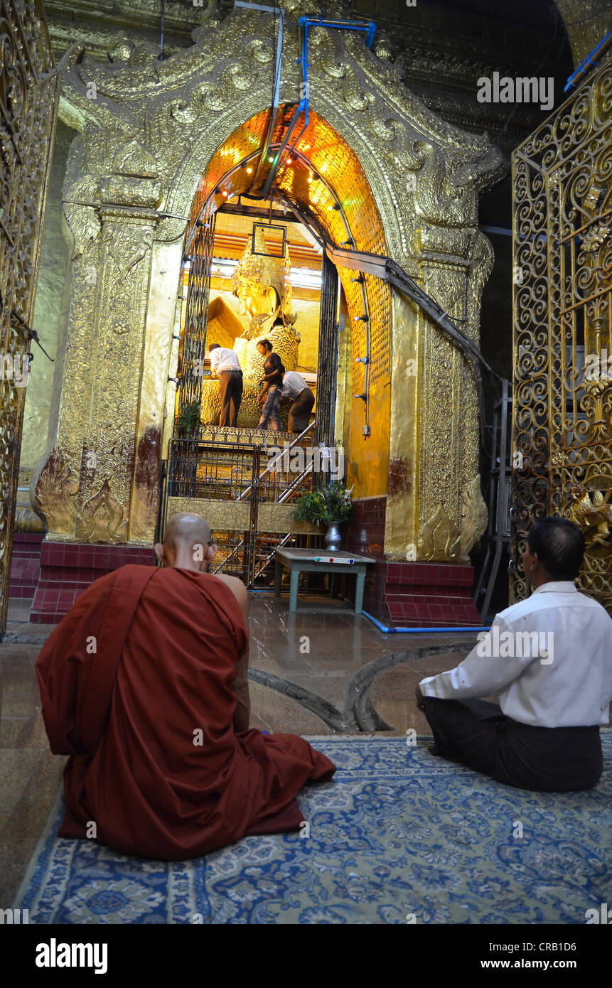 Burmese monk and a devout elderly man sitting in prayer in front of the ...