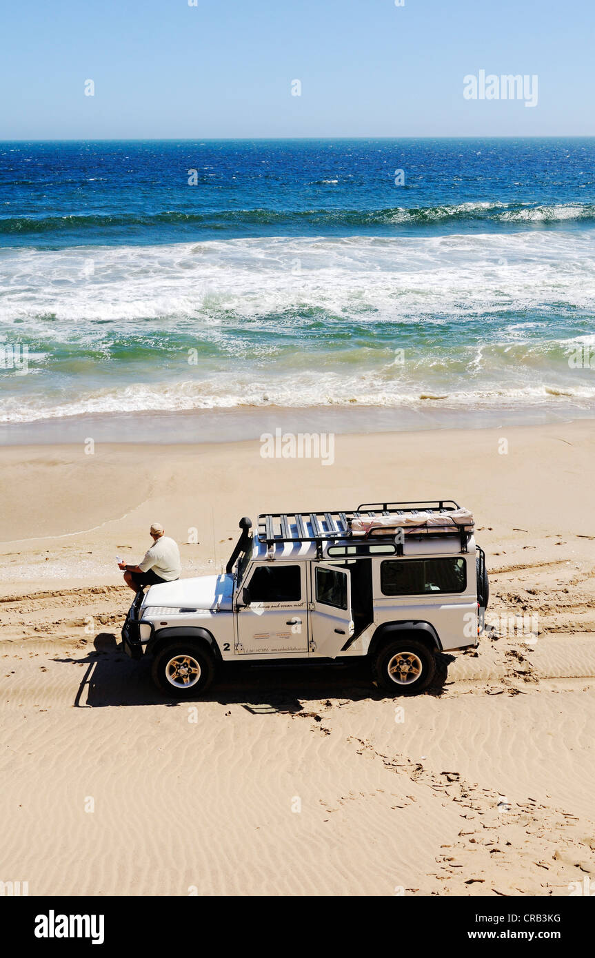Man sitting on a Landrover Defender off-road vehicle on a beach, on the ...