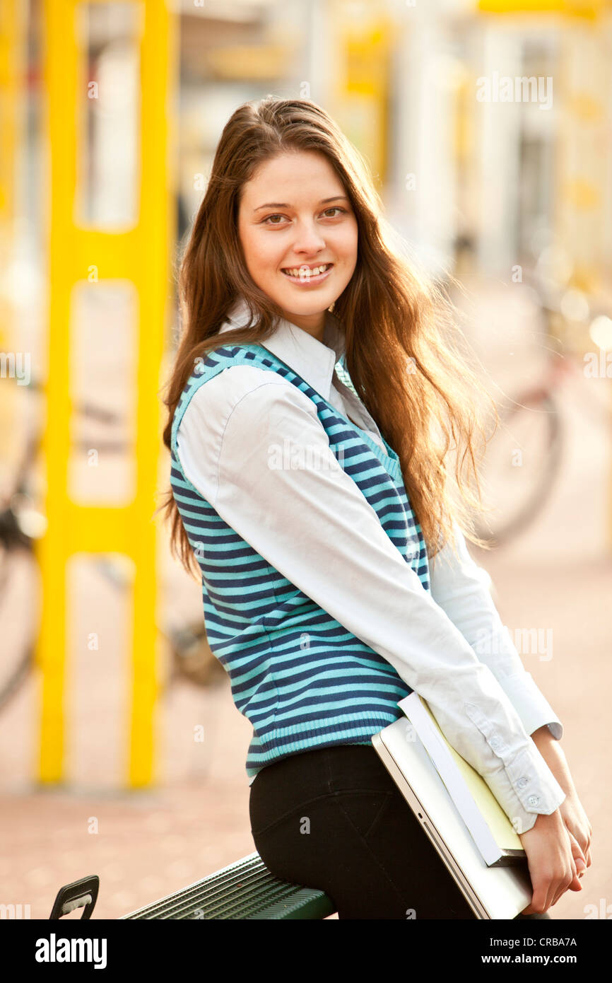 Student with a laptop and a workbook under her arm, smiling Stock Photo ...