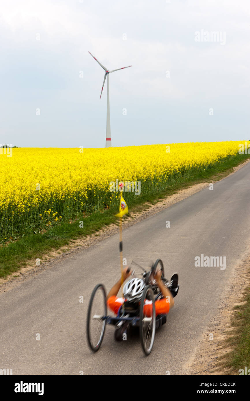 Recumbent bicycle in front of a canola field, wind turbine, wind energy ...