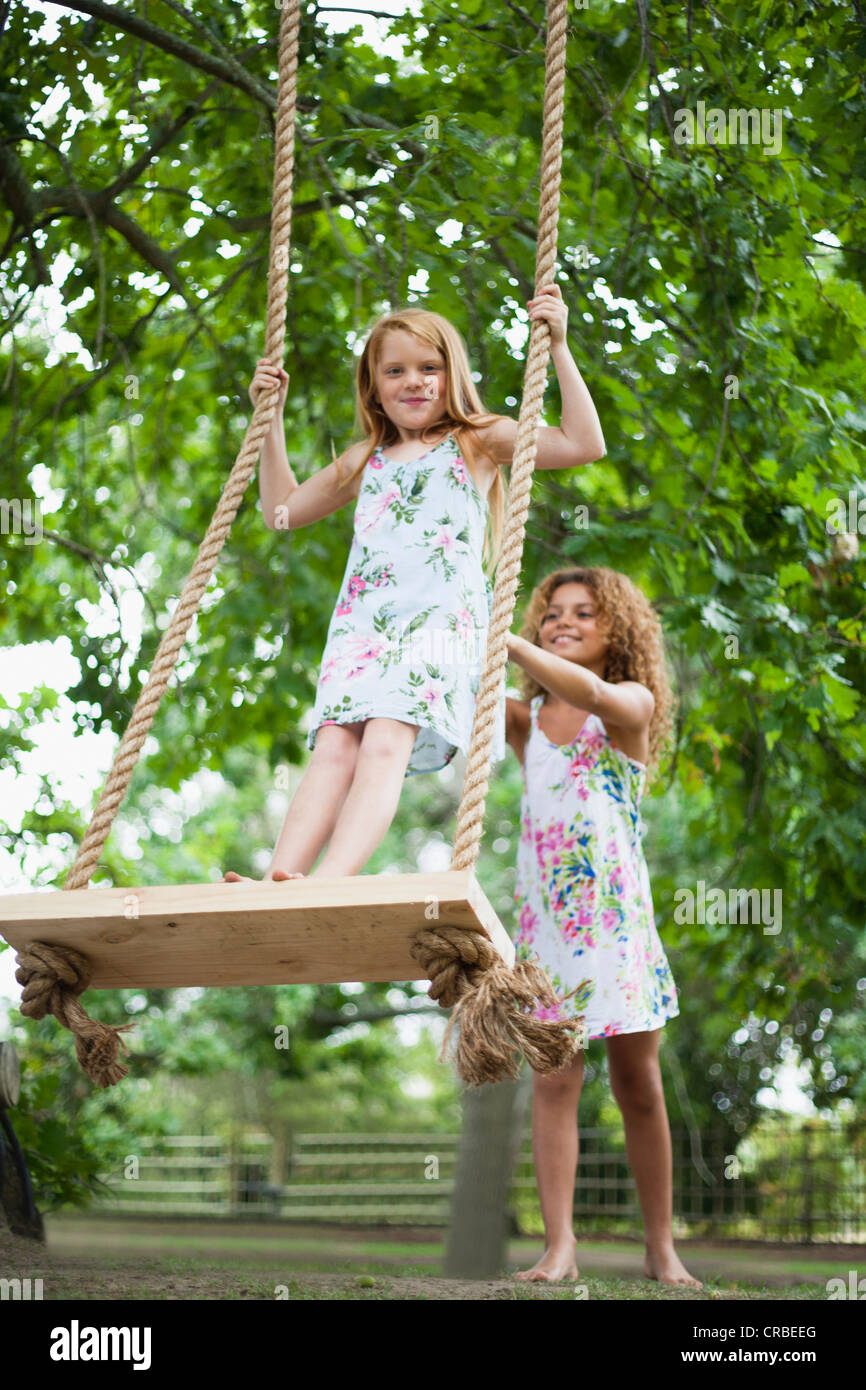 Girl pushing friend on tree swing Stock Photo - Alamy