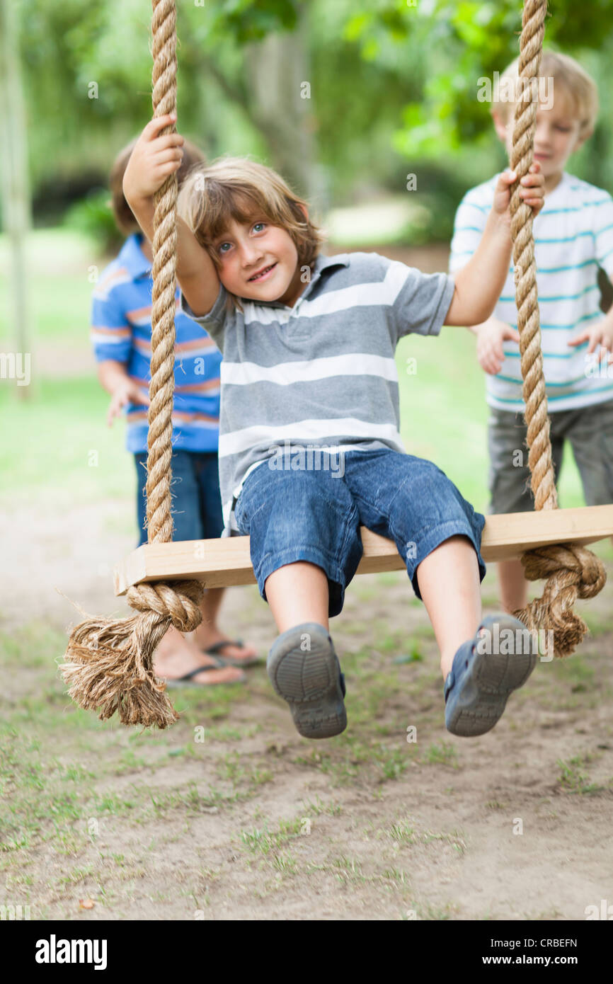Boys pushing friend on tree swing Stock Photo - Alamy