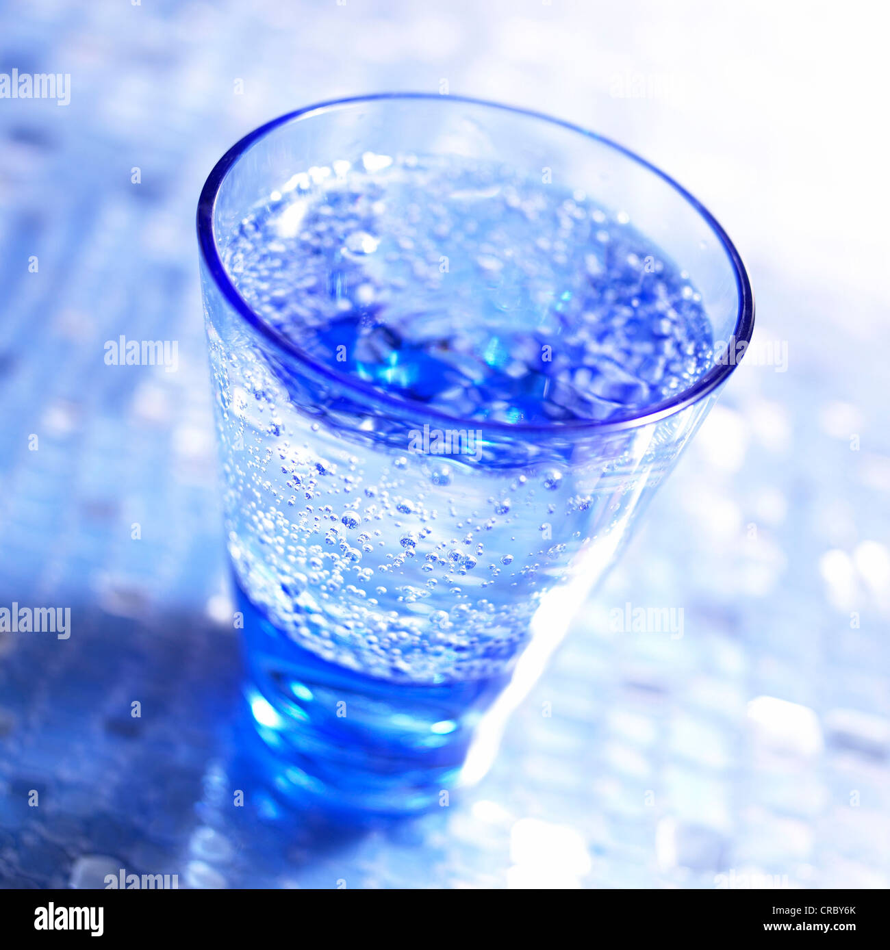 A blue glass of sparkling water on a blue shimmering textured surface ...