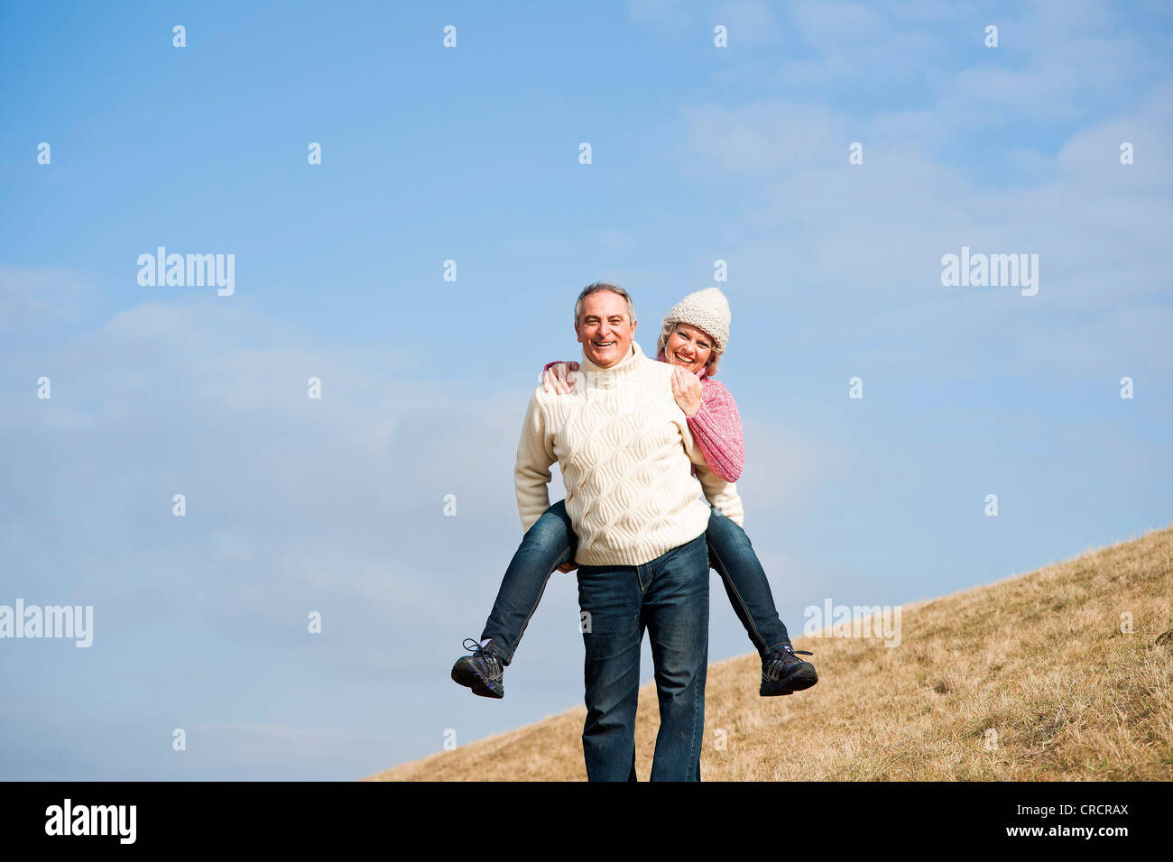 Smiling man carrying woman piggyback in meadow Stock Photo - Alamy
