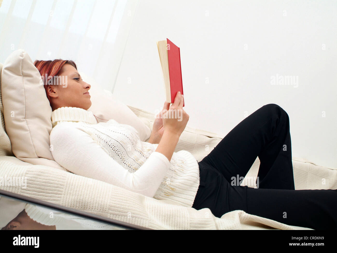 young woman on couch, reading a book Stock Photo - Alamy