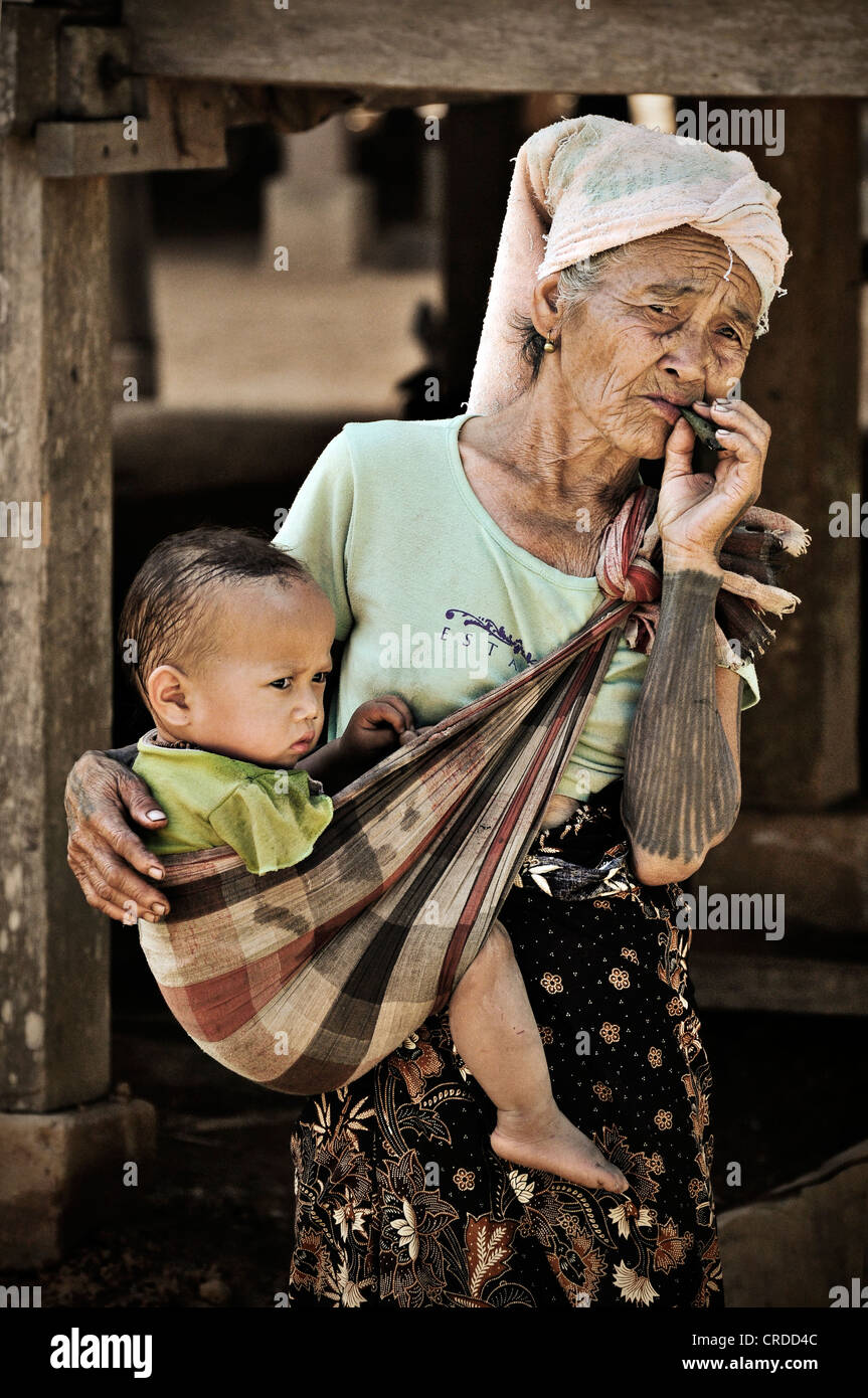 Old woman, grandmother smoking a cigar, carrying a toddler in a baby ...