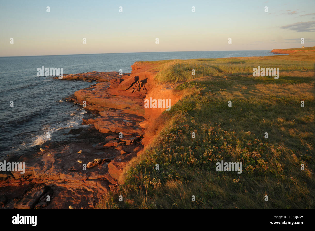 With the sun setting, the red cliffs of Prince Edward Island provide a ...