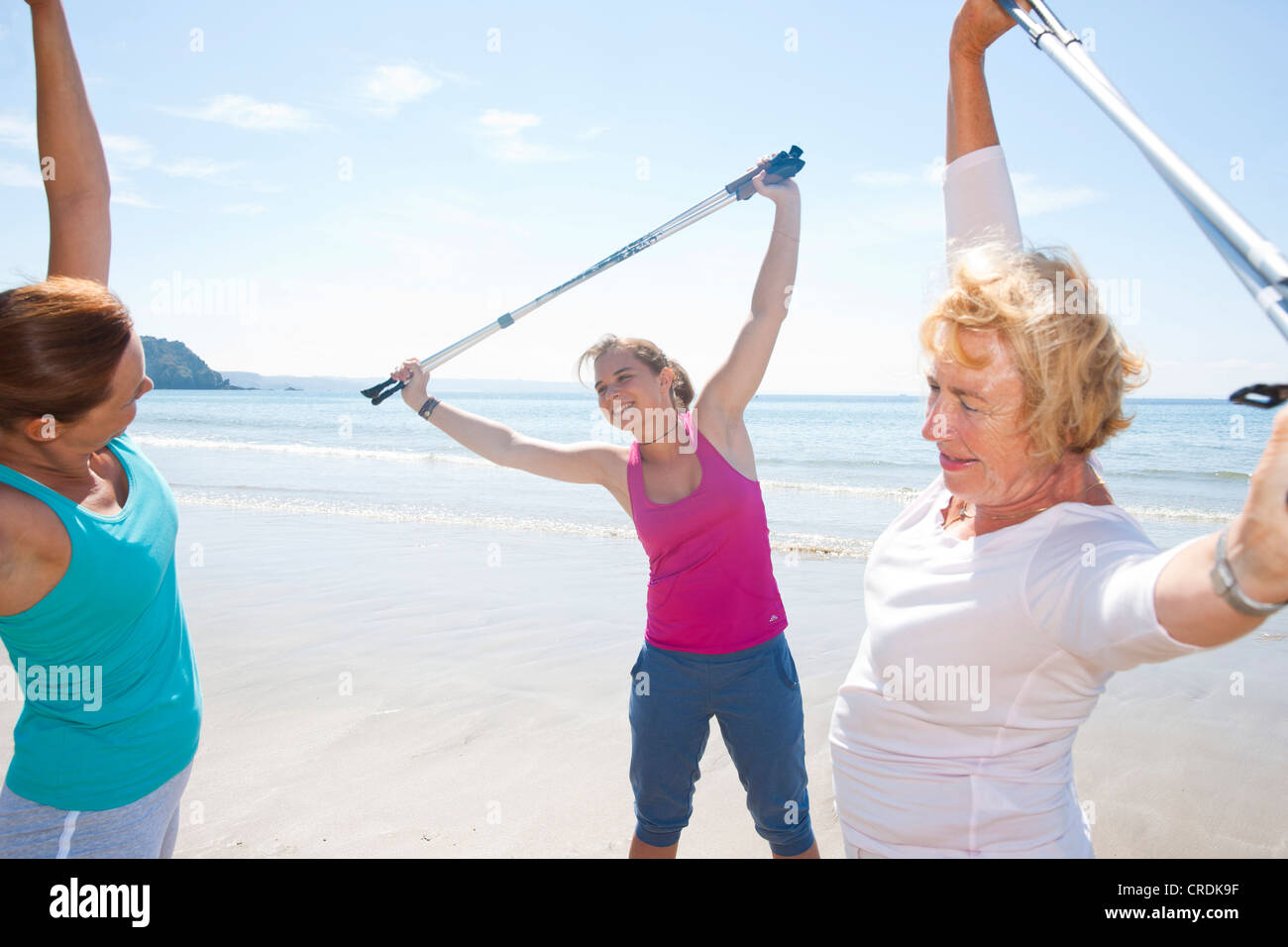 Three women doing stretching exercises with walking sticks on the beach ...