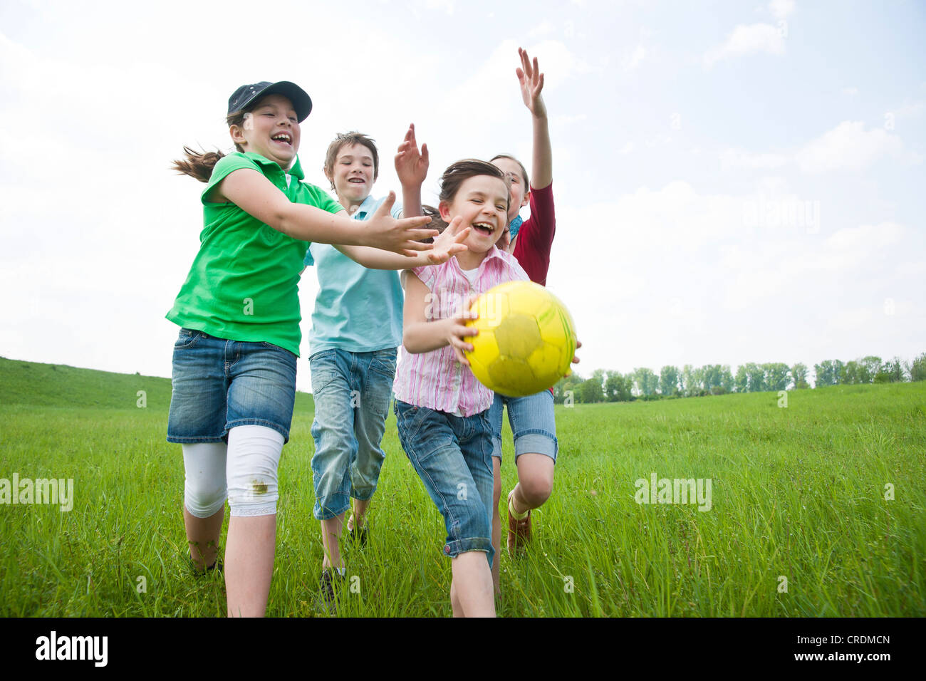 Four friends, three girls and a boy playing ball in a meadow Stock ...