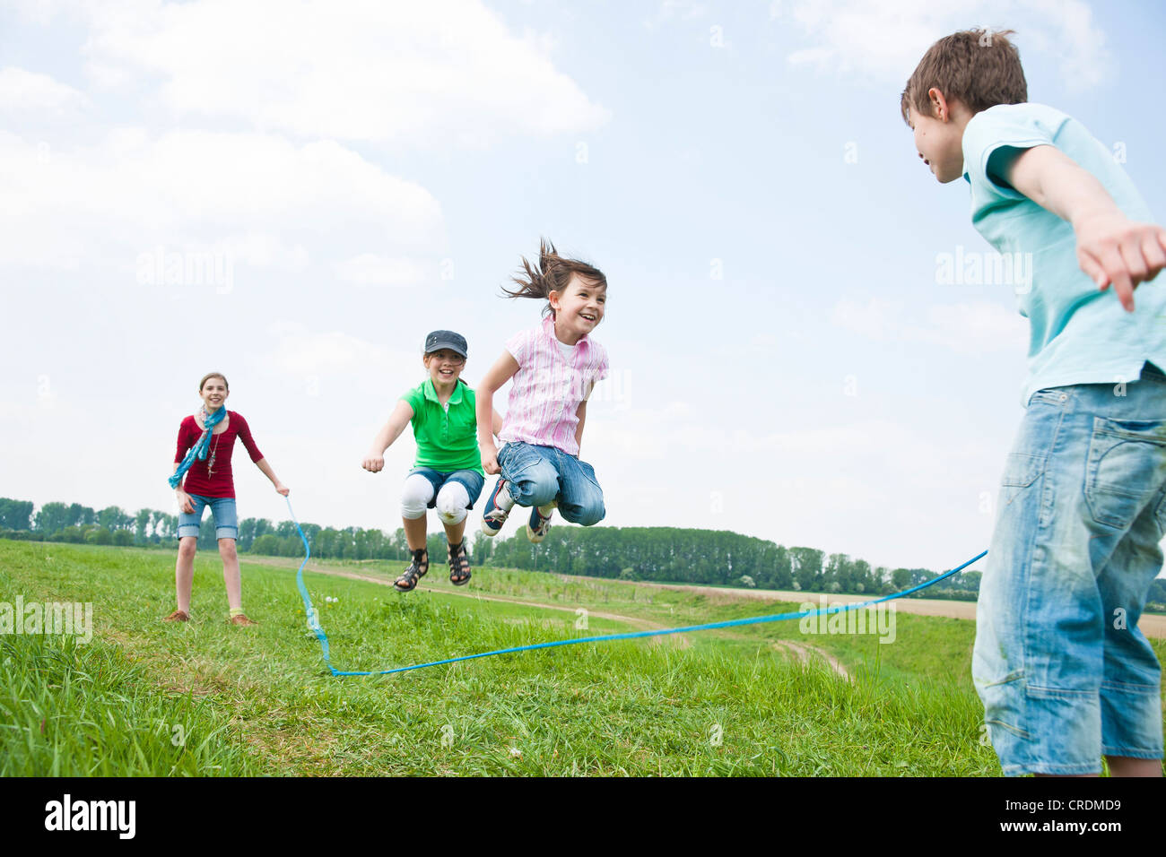 Four friends, three girls and a boy jumping ropes in a meadow Stock ...