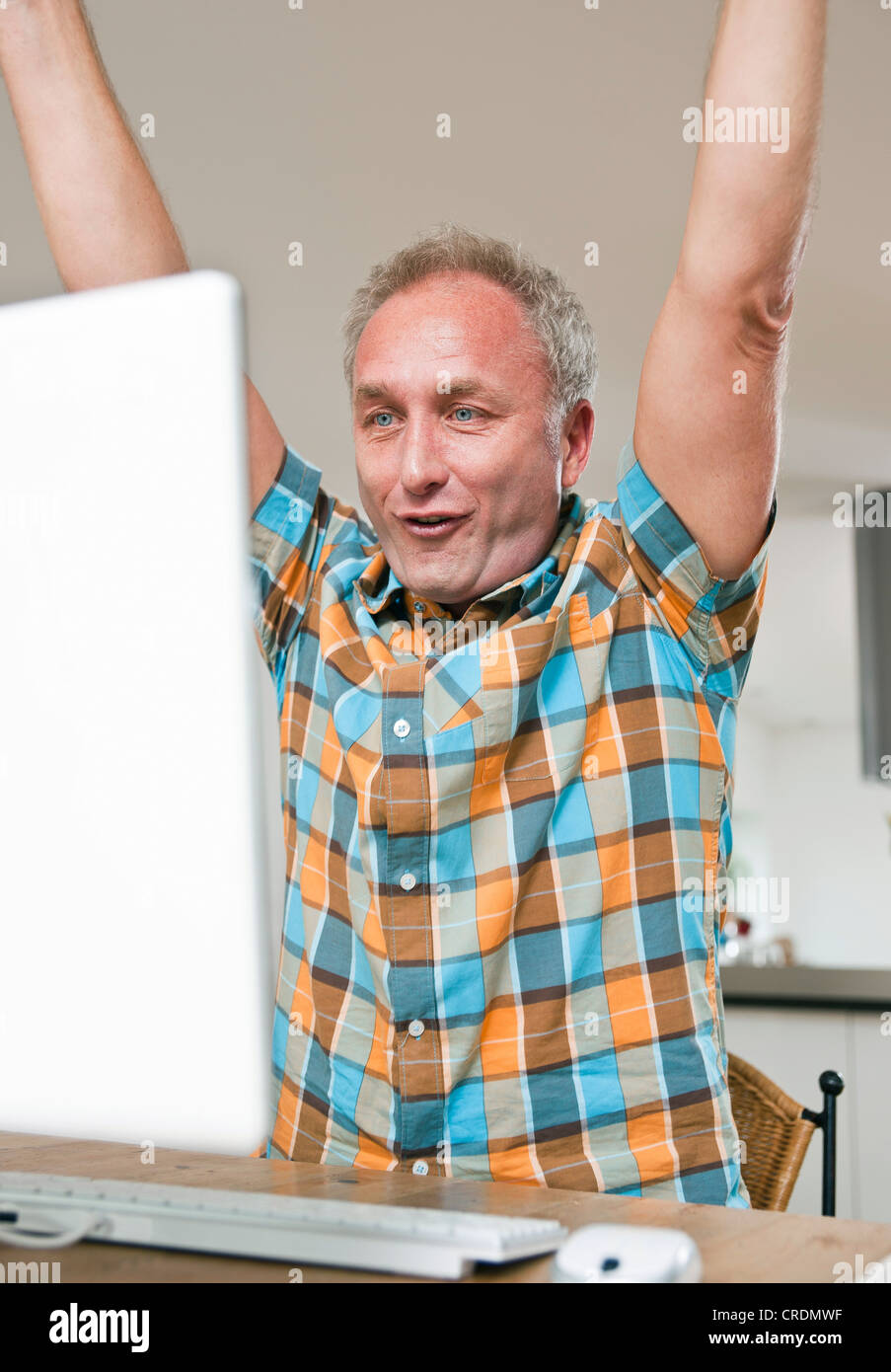 Man sitting in front of a computer, cheering Stock Photo - Alamy