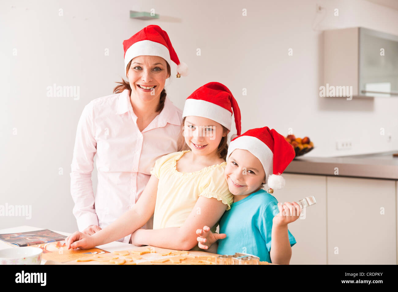 Two girls and their mother baking Christmas cookies while wearing Santa ...