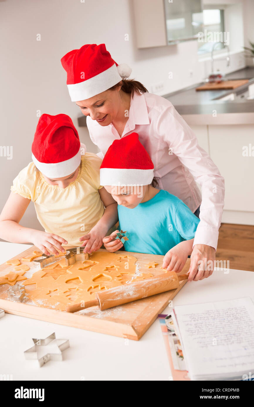 Two girls and their mother baking Christmas cookies while wearing Santa ...