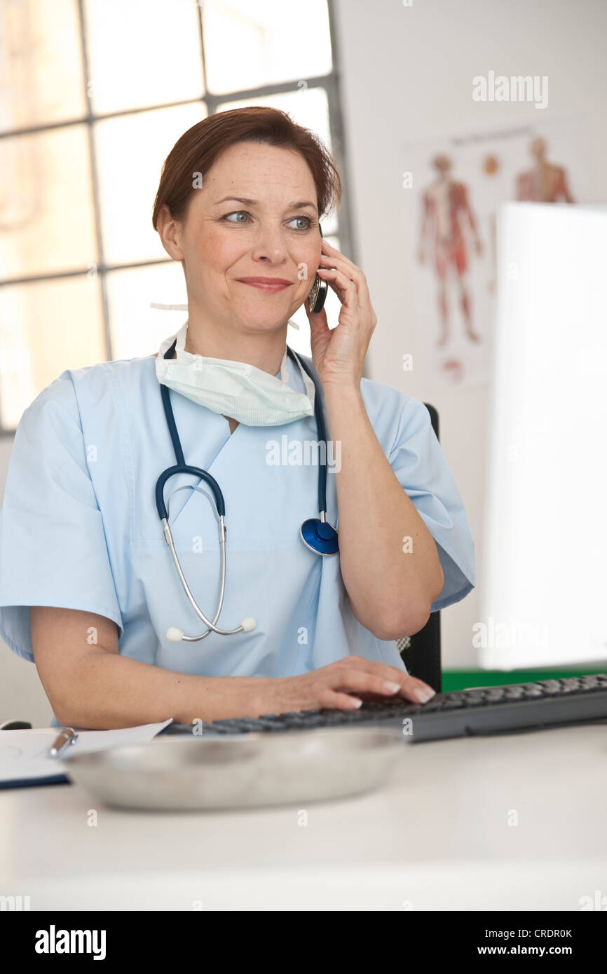 Female doctor sitting in front of a computer and talking on a telephone ...