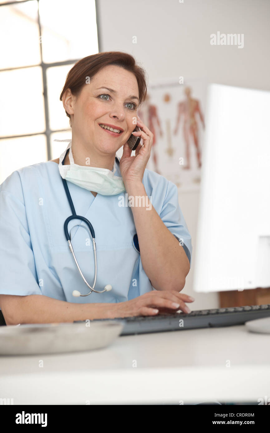 Female doctor sitting in front of a computer and talking on a telephone ...
