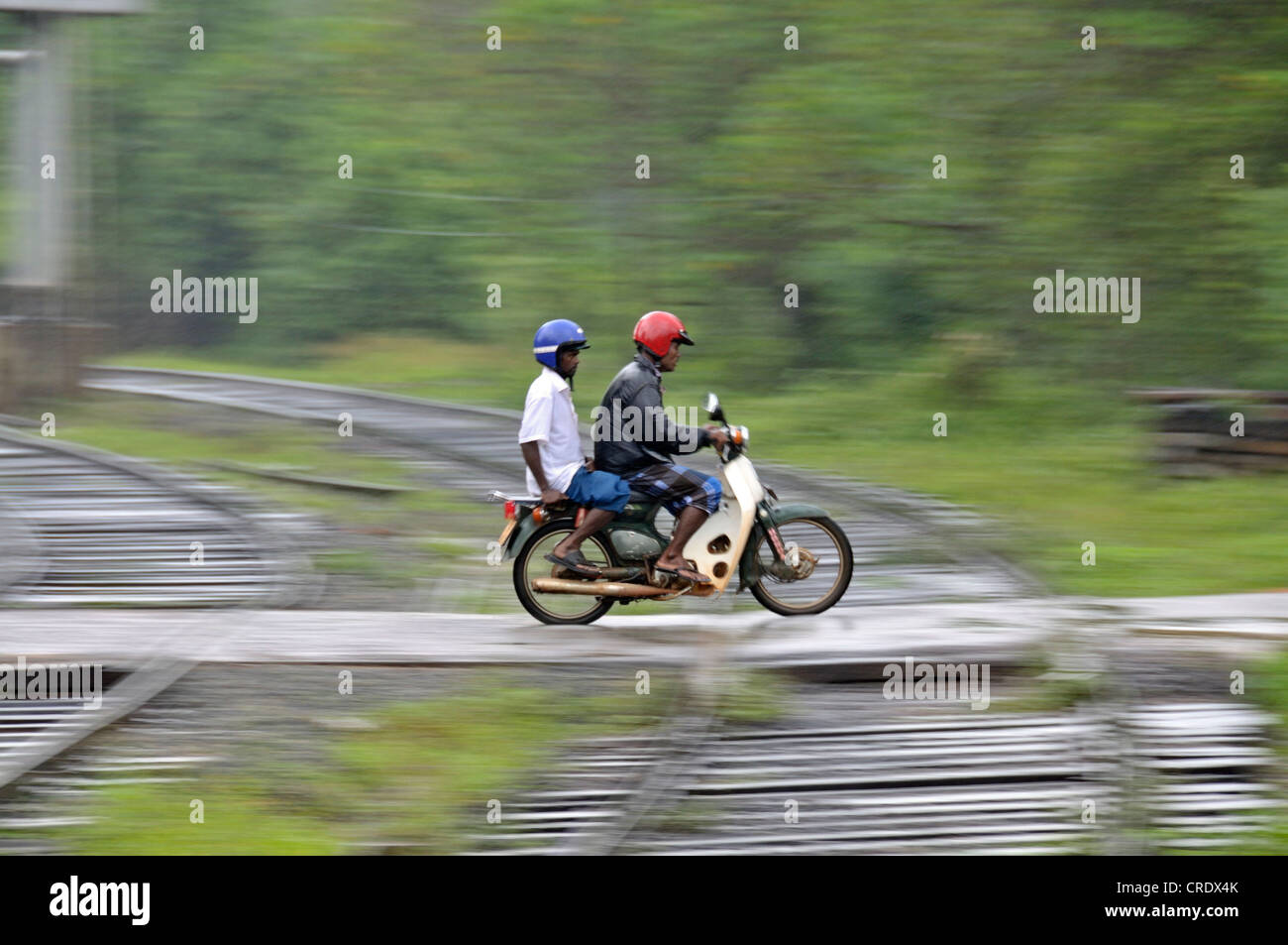 Moped riders in heavy rain, railway crossing in Kalawewa, Sri Lanka ...