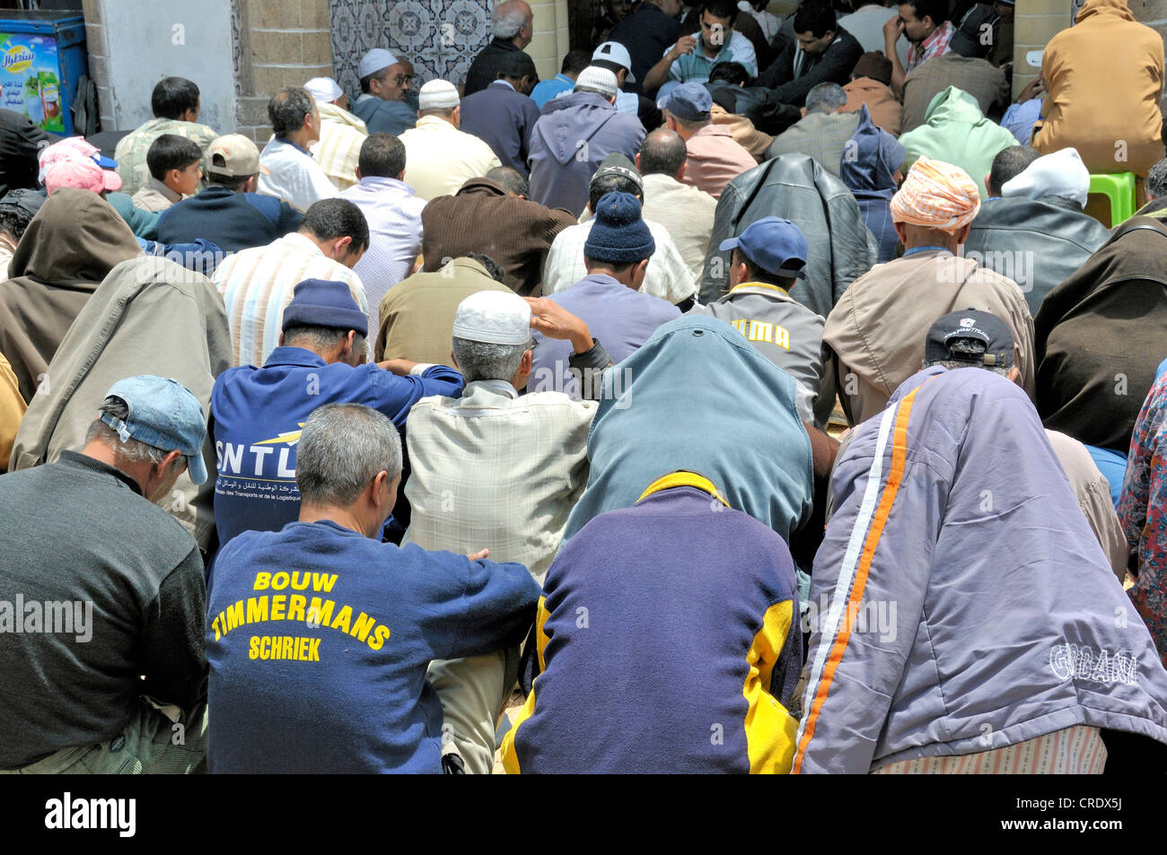 Men sitting in a street in front of a crowded mosque during Friday ...