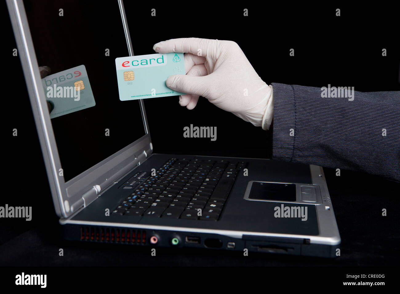 Hacker using a laptop, holding a health insurance card, symbolic image ...