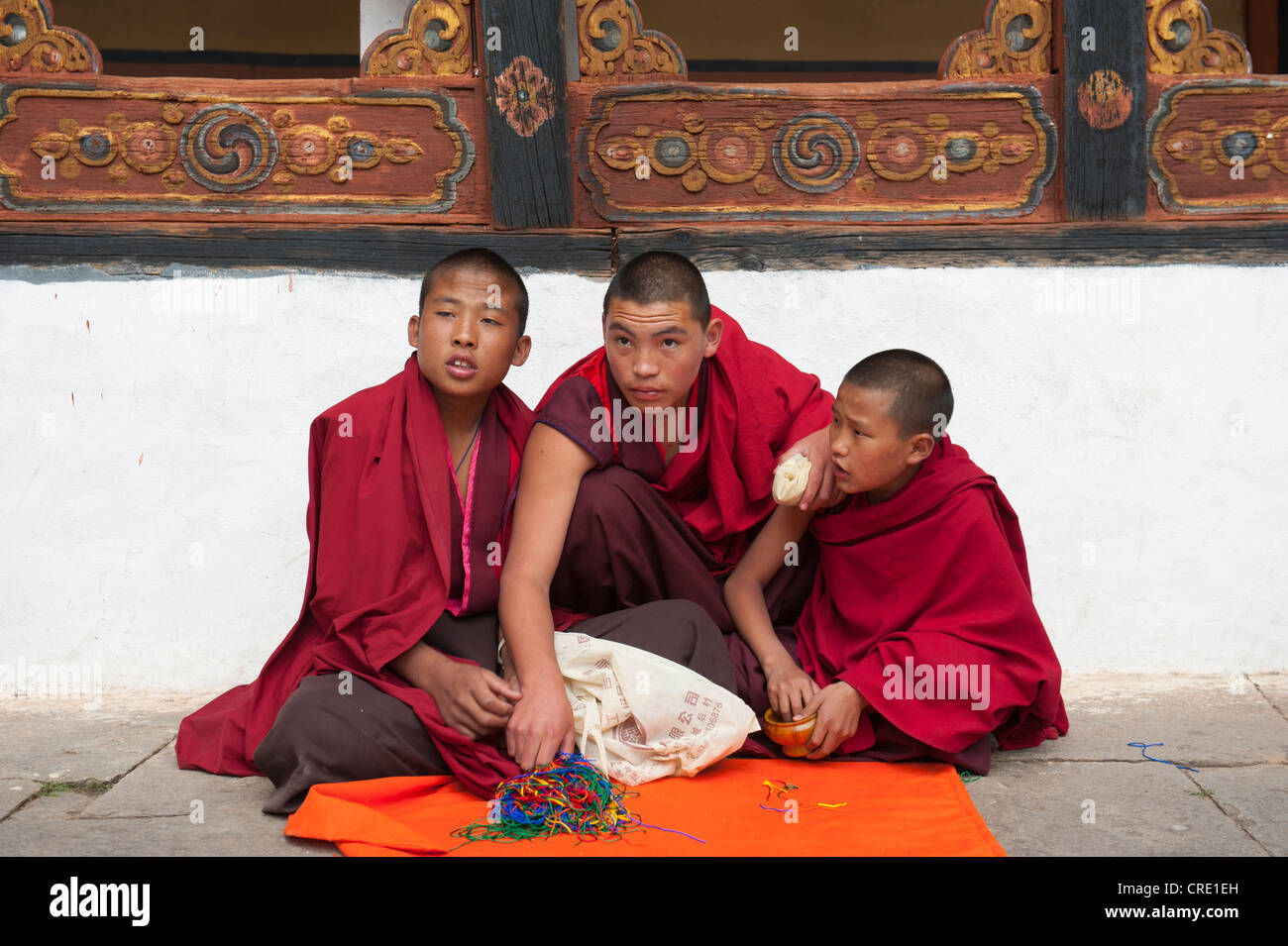 Tibetan Buddhism, three novices sitting on the ground wearing red robes ...
