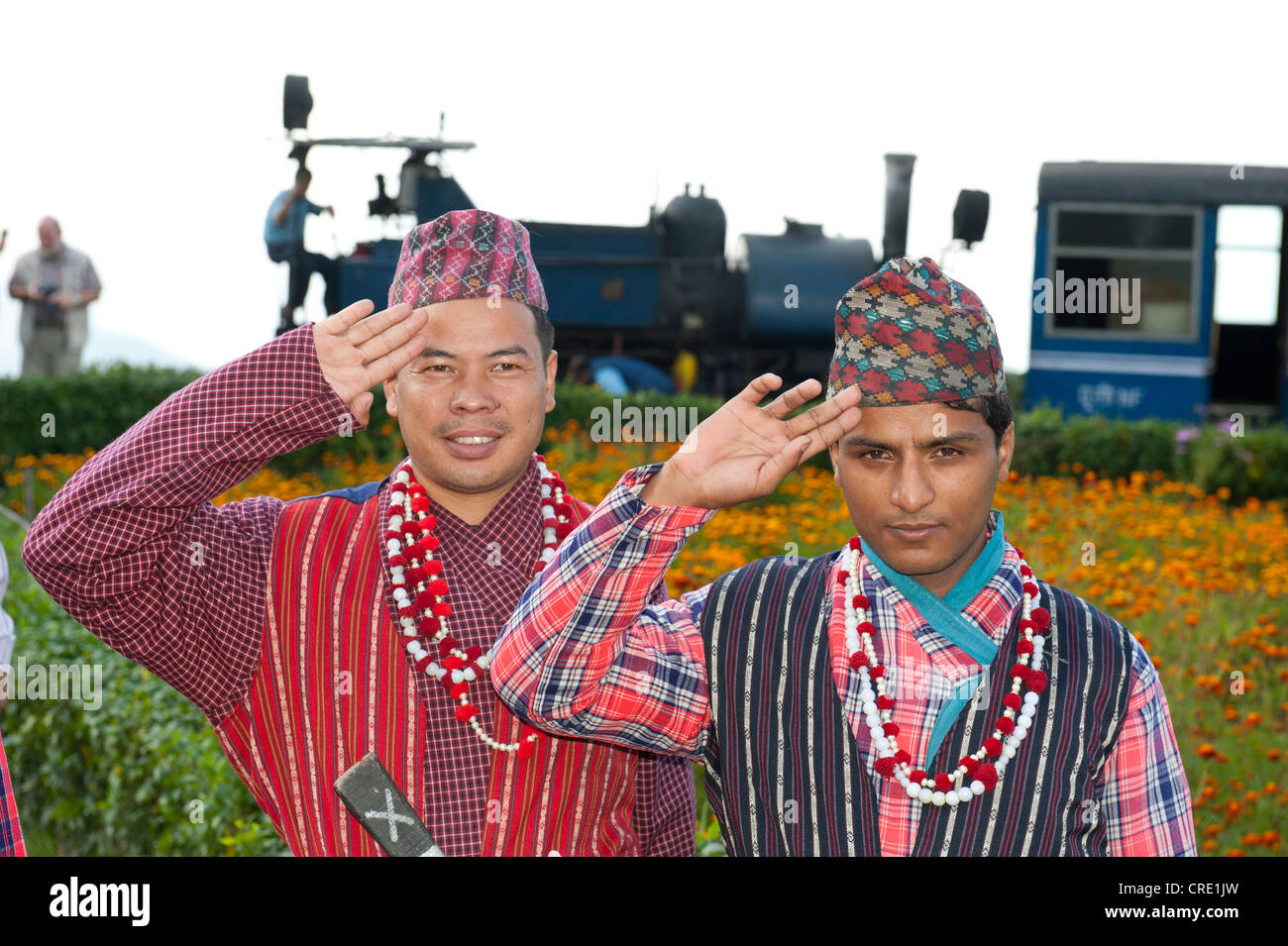 Two Nepali men in traditional costume saluting, historic train at back ...