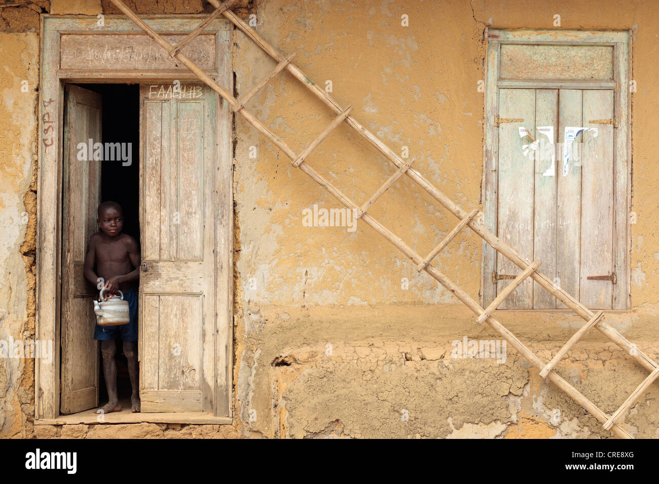 A boy comes out of a home holding a plastic teapot typically used for ...