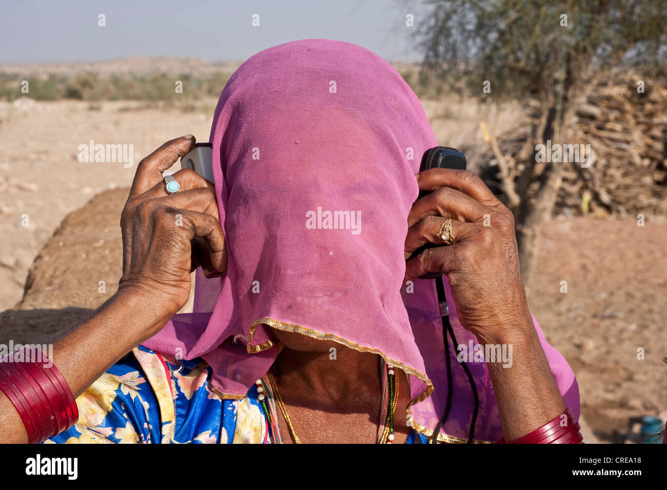 Veiled Indian woman speaking on two mobile phones simultaneously, Thar ...