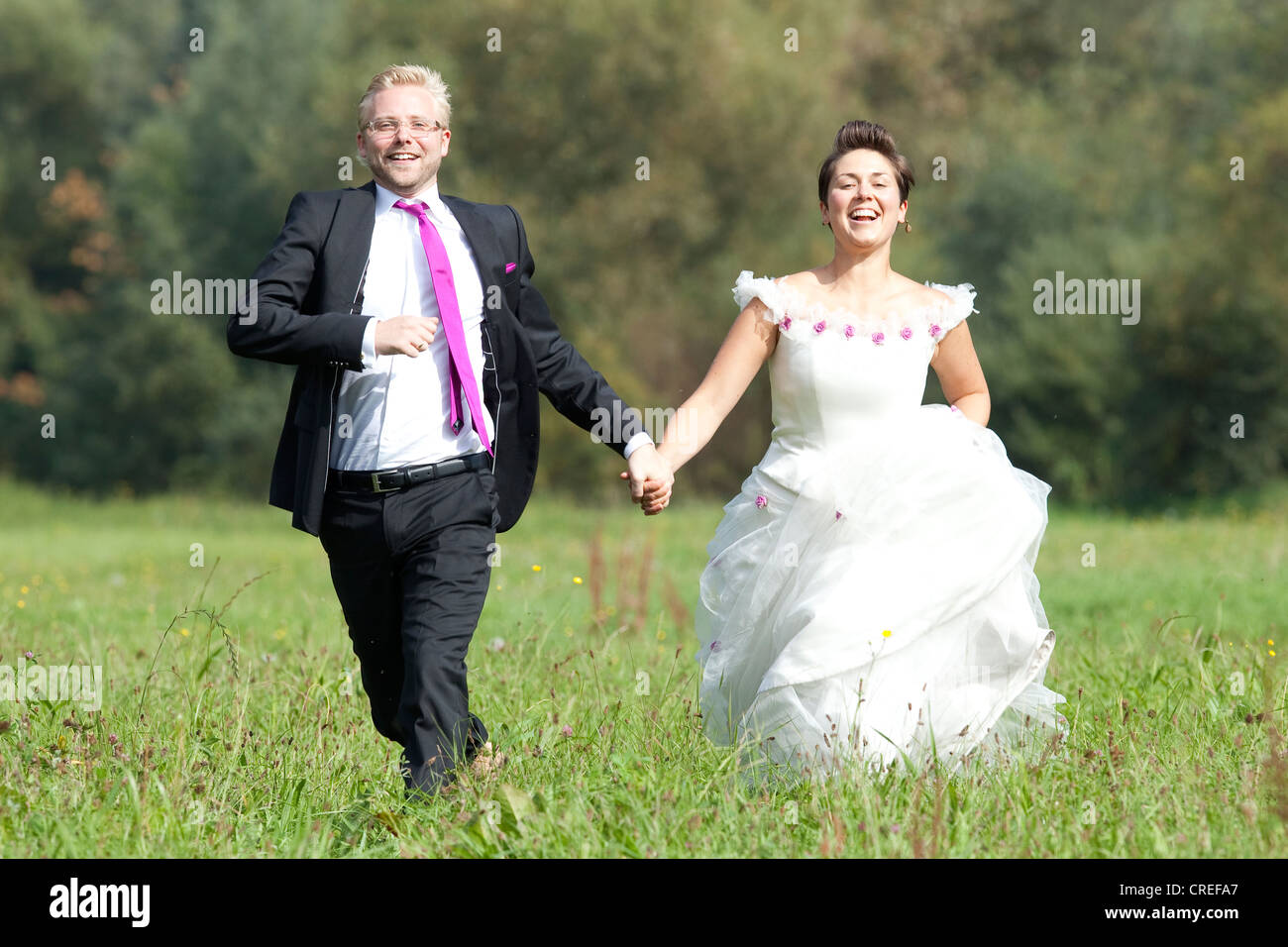 Bride and groom running across a meadow, Regensburg, Bavaria, Germany ...