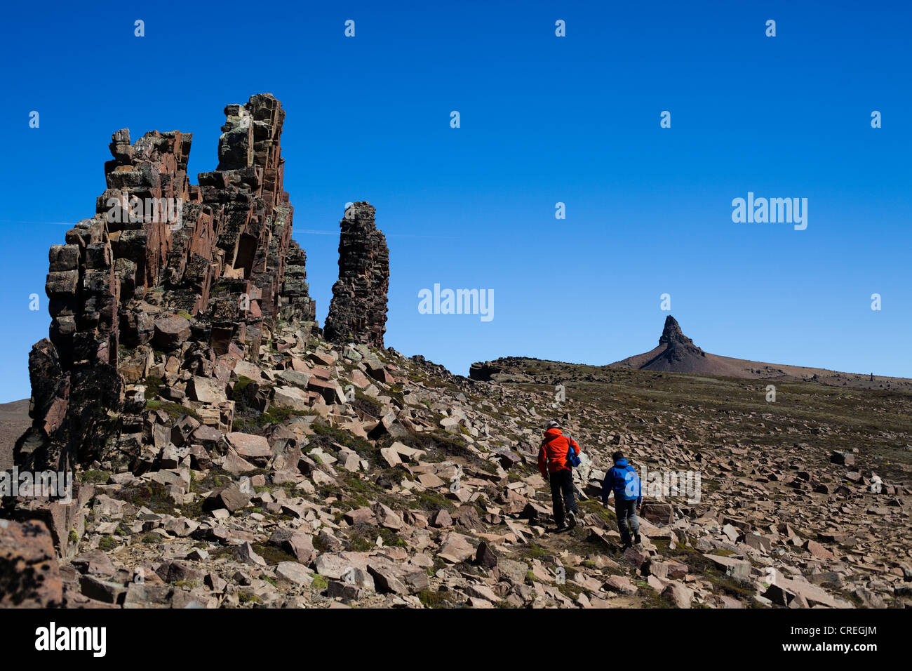 Two hikers walk through a rocky field with a unique wall of crumbling ...