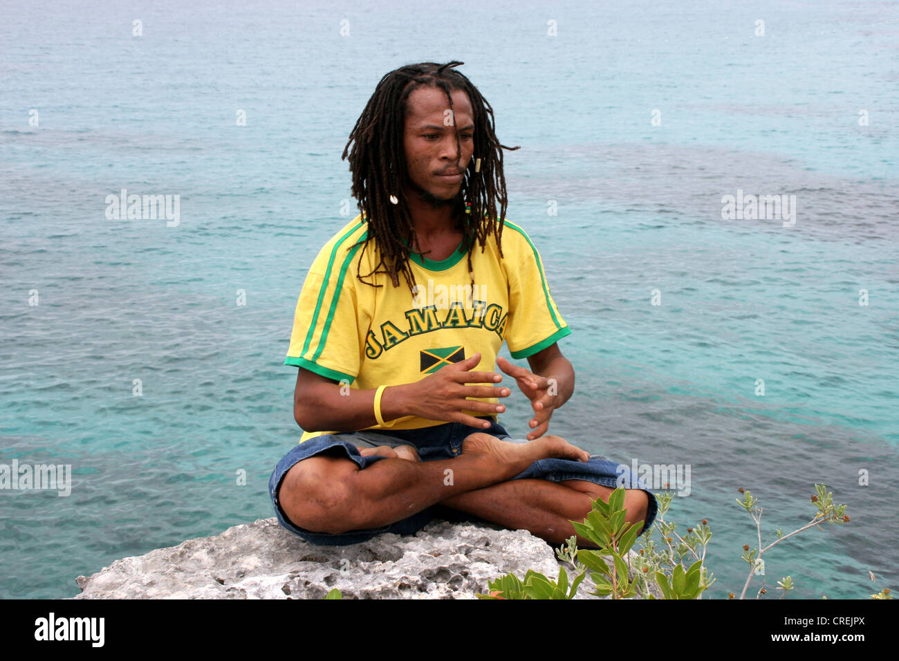 Rasta man with Rasta curls and shirt in the national colors meditating ...