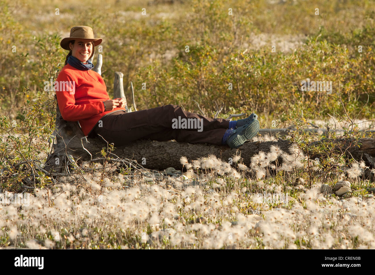 Young woman relaxing, enjoying evening light, sitting on a tree trunk ...