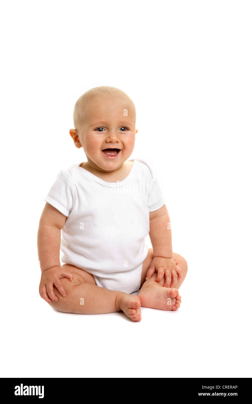 A bright seven month old baby boy sitting upright with hands on knees ...
